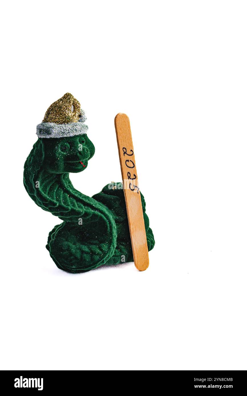 Green snake figurine in a hat with a wooden stick 2025 on a white ...
