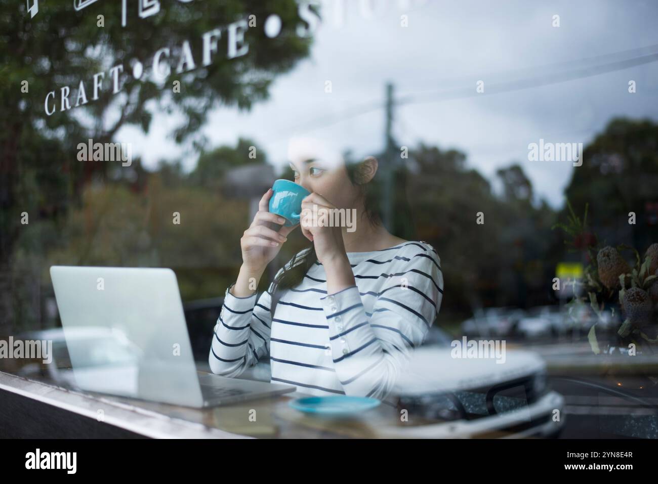 Woman through window glass opening computer in café Stock Photo - Alamy