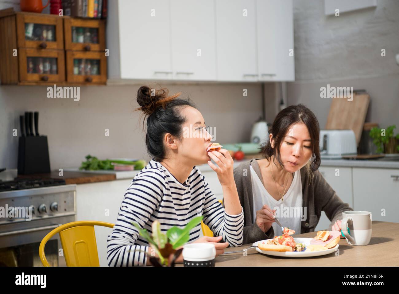 Two women eating rice in the kitchen Stock Photo - Alamy