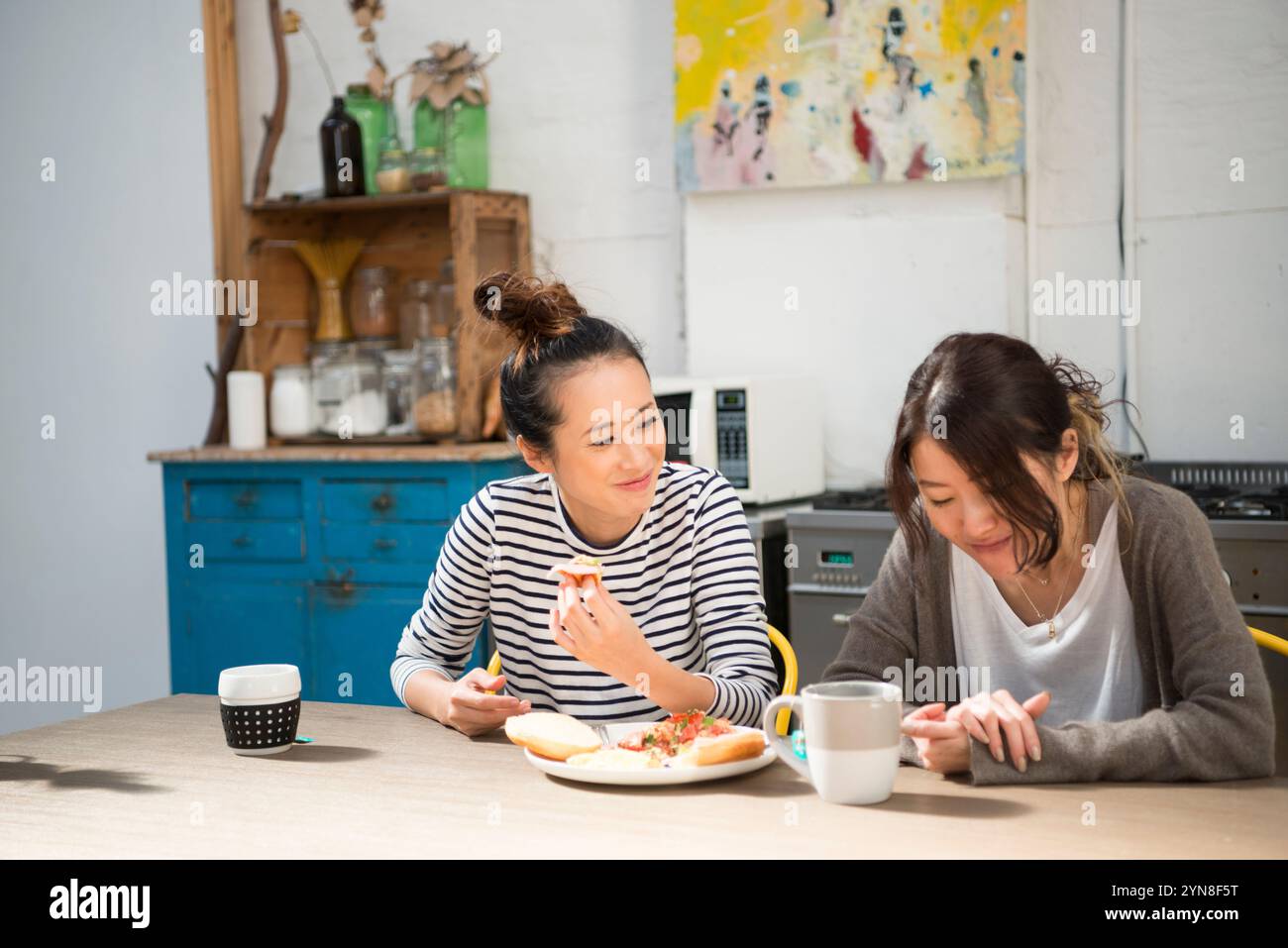 Two women eating rice in the kitchen Stock Photo - Alamy