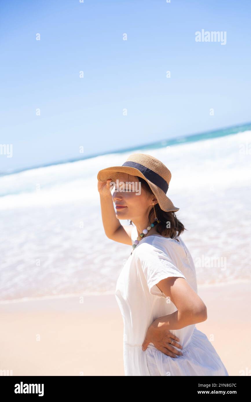 Woman walking on beach holding hat down Stock Photo - Alamy