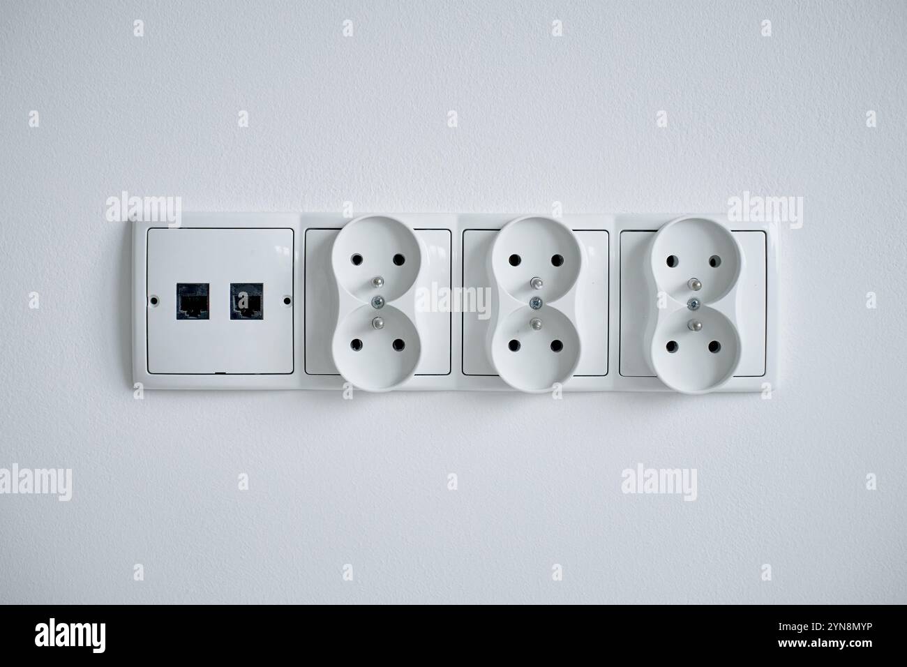 Close-up of white electrical sockets and ethernet ports on white wall ...