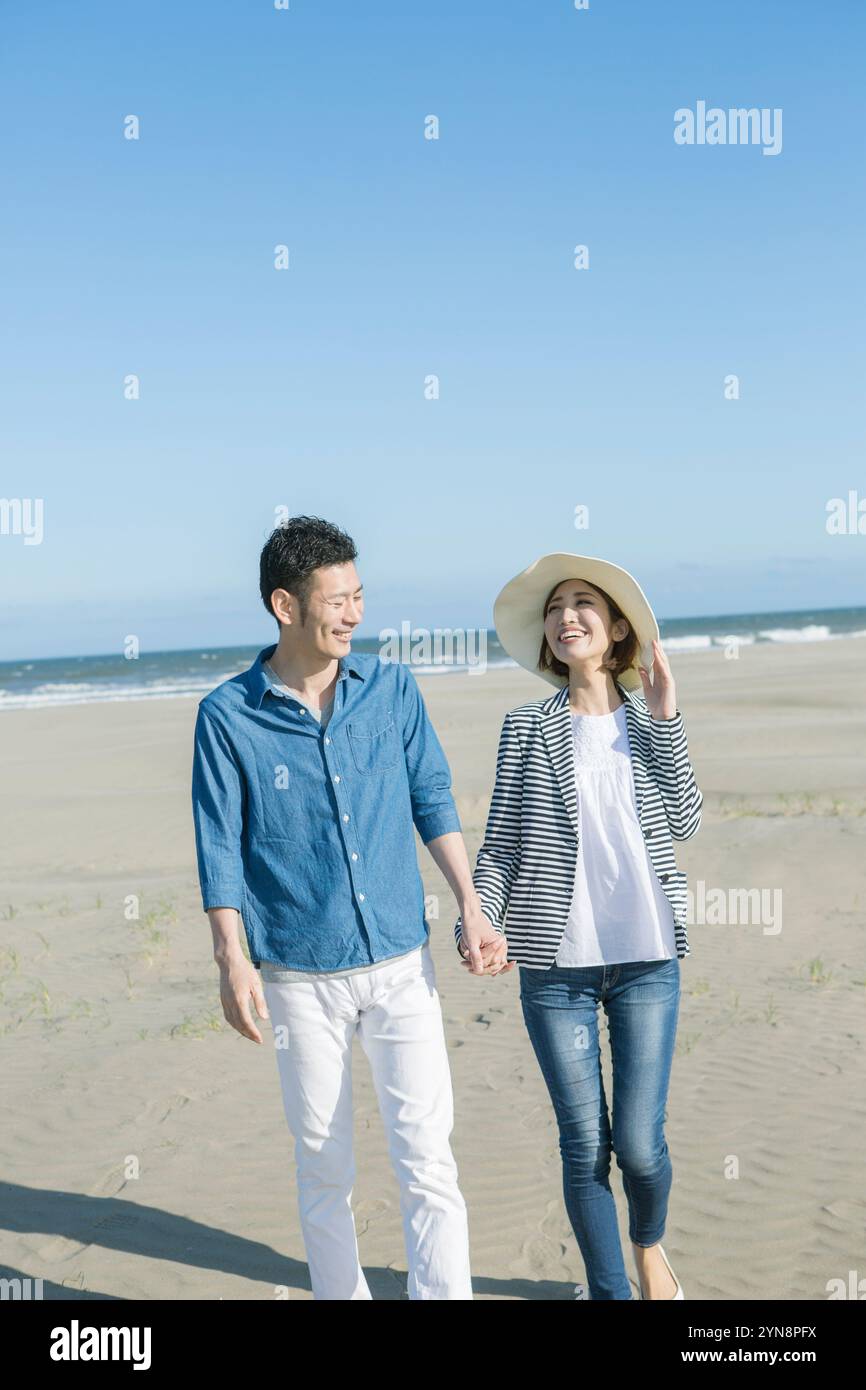 Couple in their 20s and 30s walking along the beach smiling Stock Photo ...
