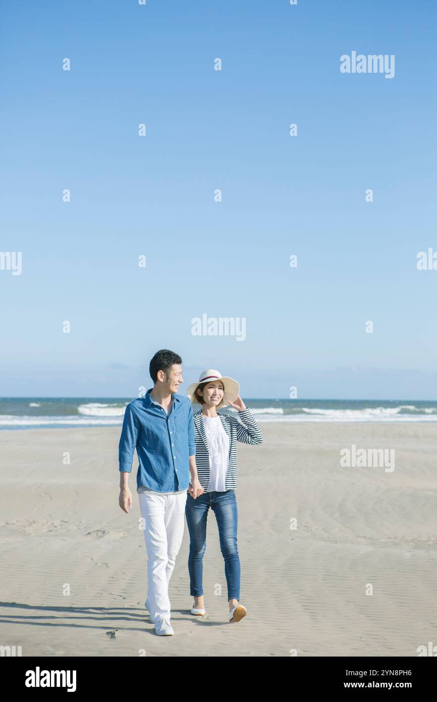 Couple in their 20s and 30s walking along the beach smiling Stock Photo ...