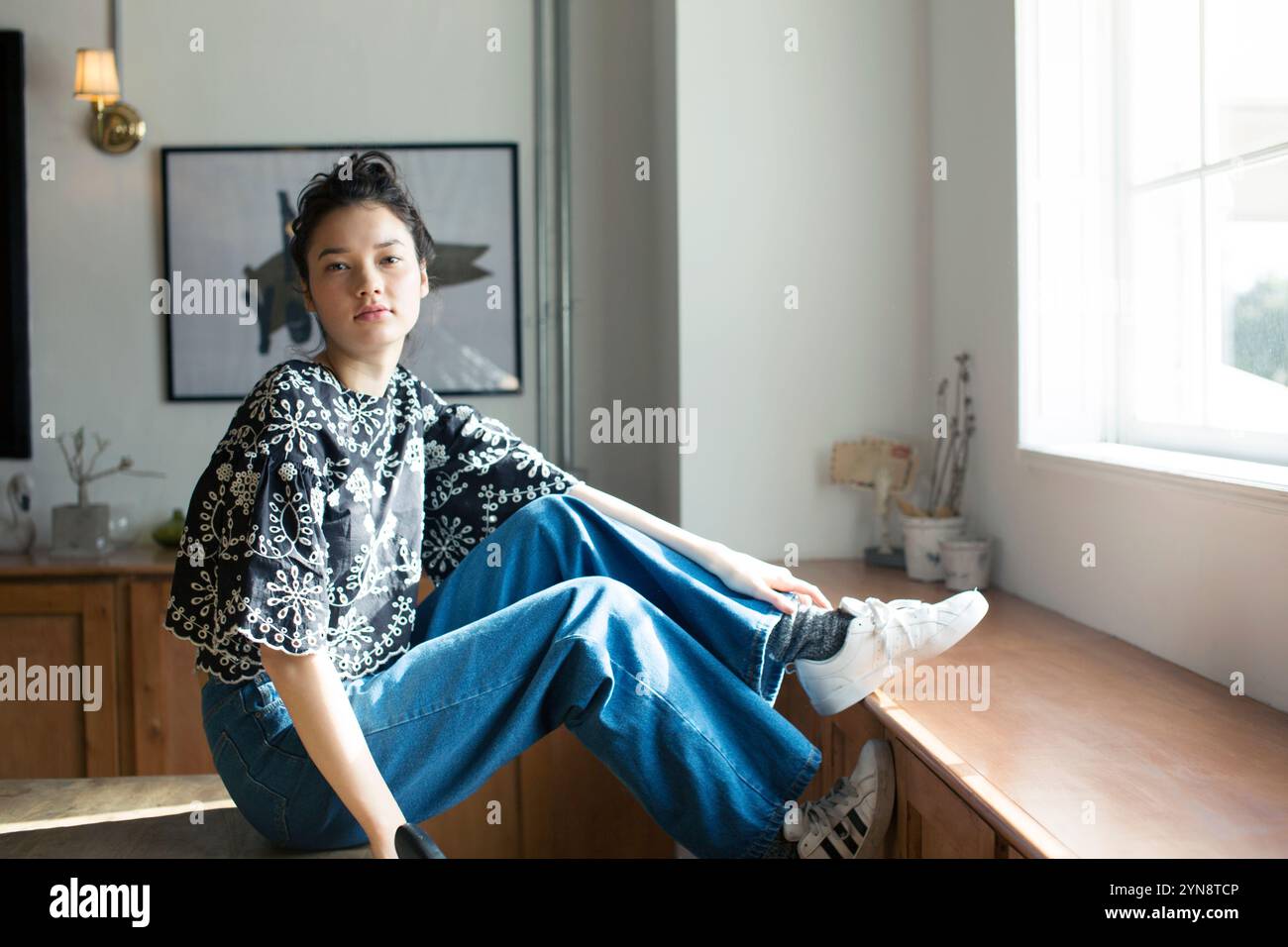 Cool-looking woman in her 20s sitting on desk Stock Photo - Alamy