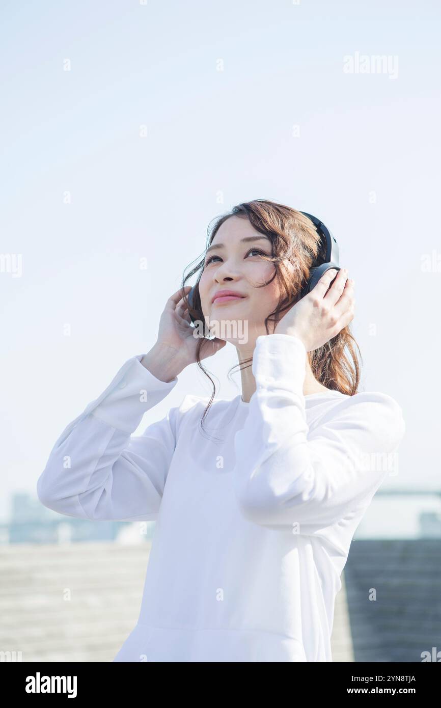 Smiling woman in her 20s putting her hand on her headphones Stock Photo ...