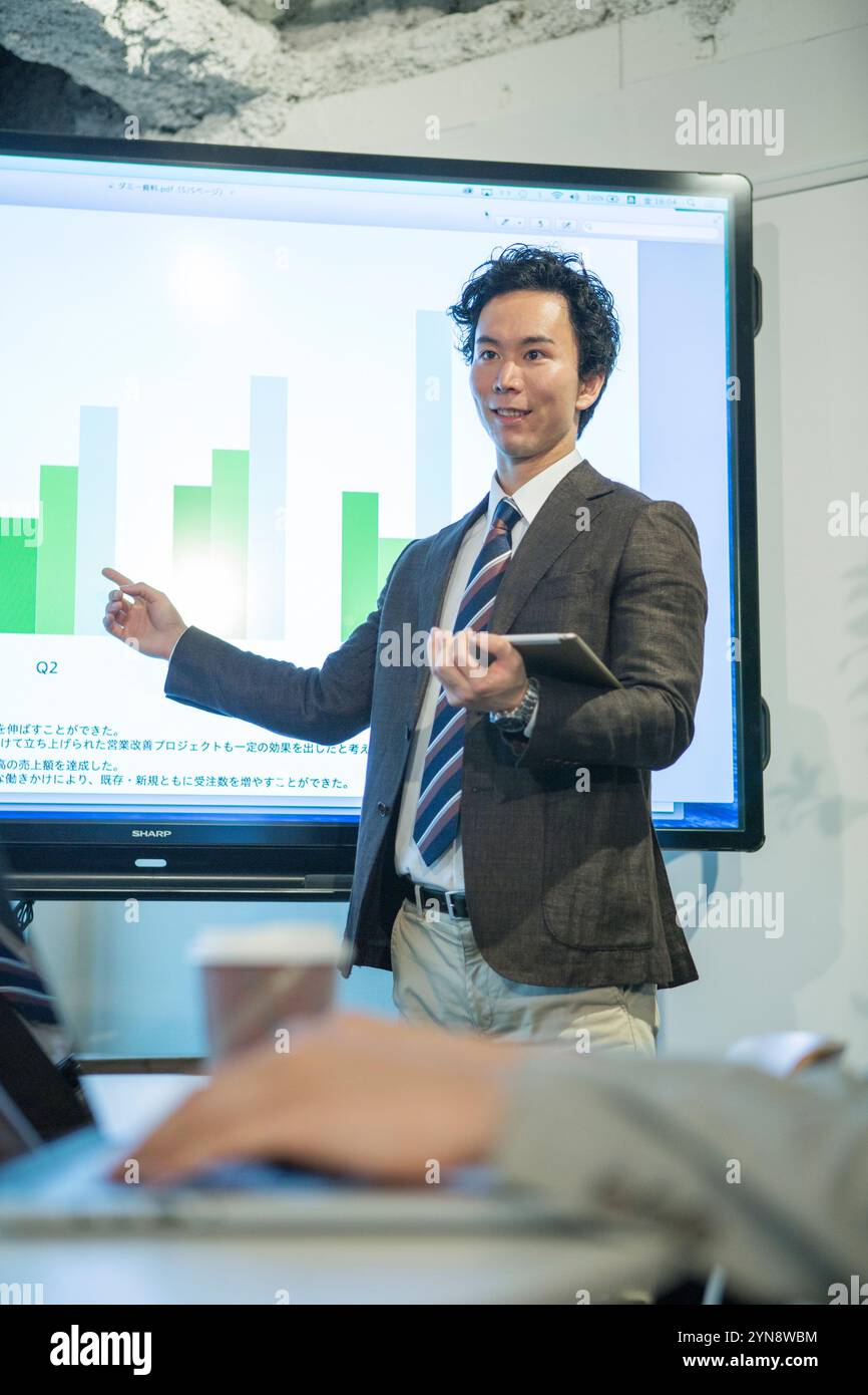 Smiling man in his 20s showing and explaining a graph Stock Photo - Alamy