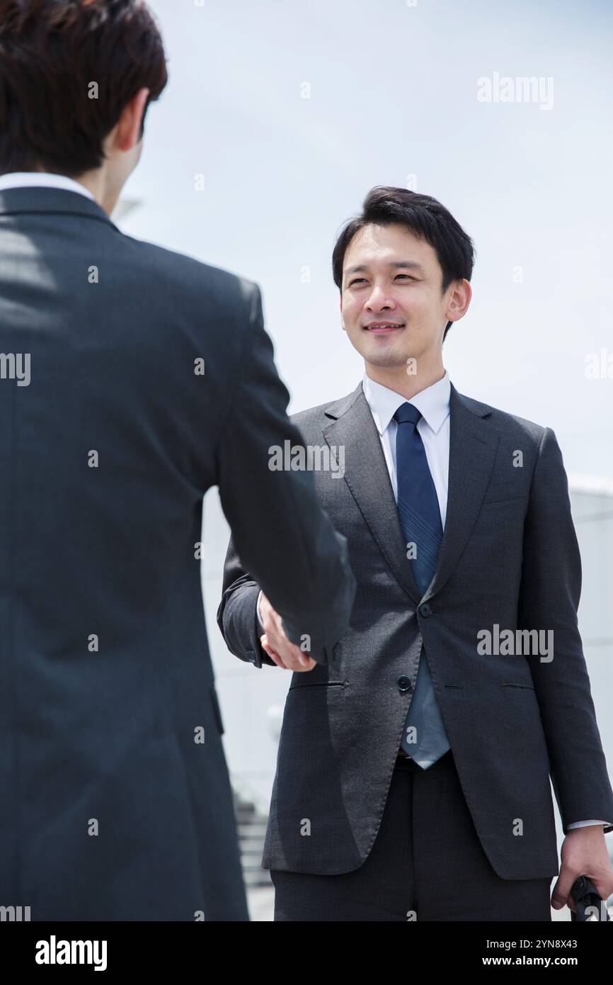 Two men in their 20s in suits shaking hands with their arms crossed ...