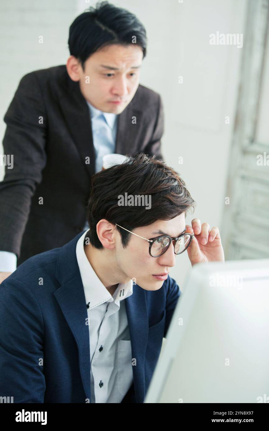 Two men in their 20s with serious expressions checking the computer ...