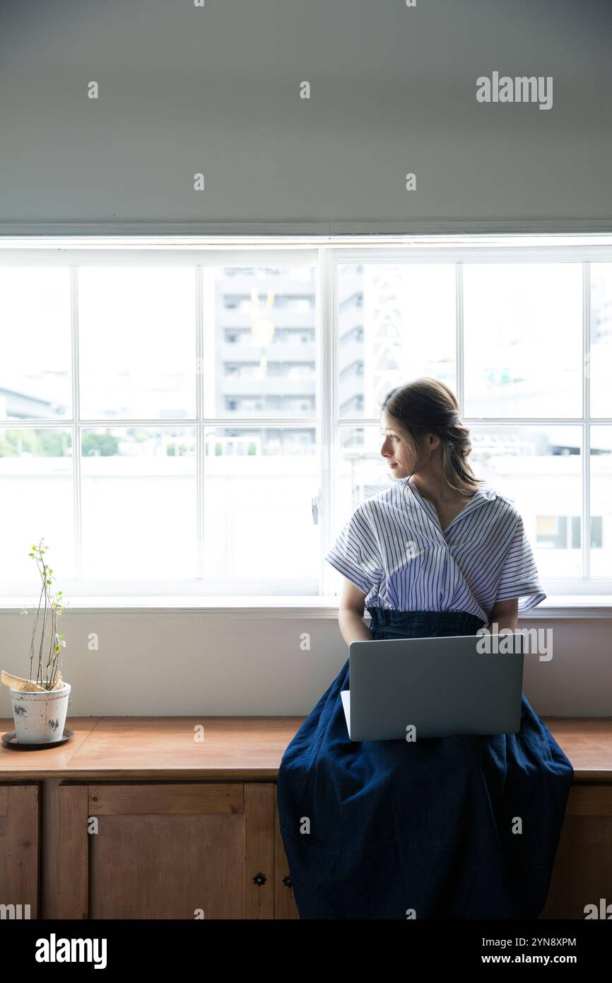 Woman in her 20s with laptop on her lap looking outside Stock Photo - Alamy