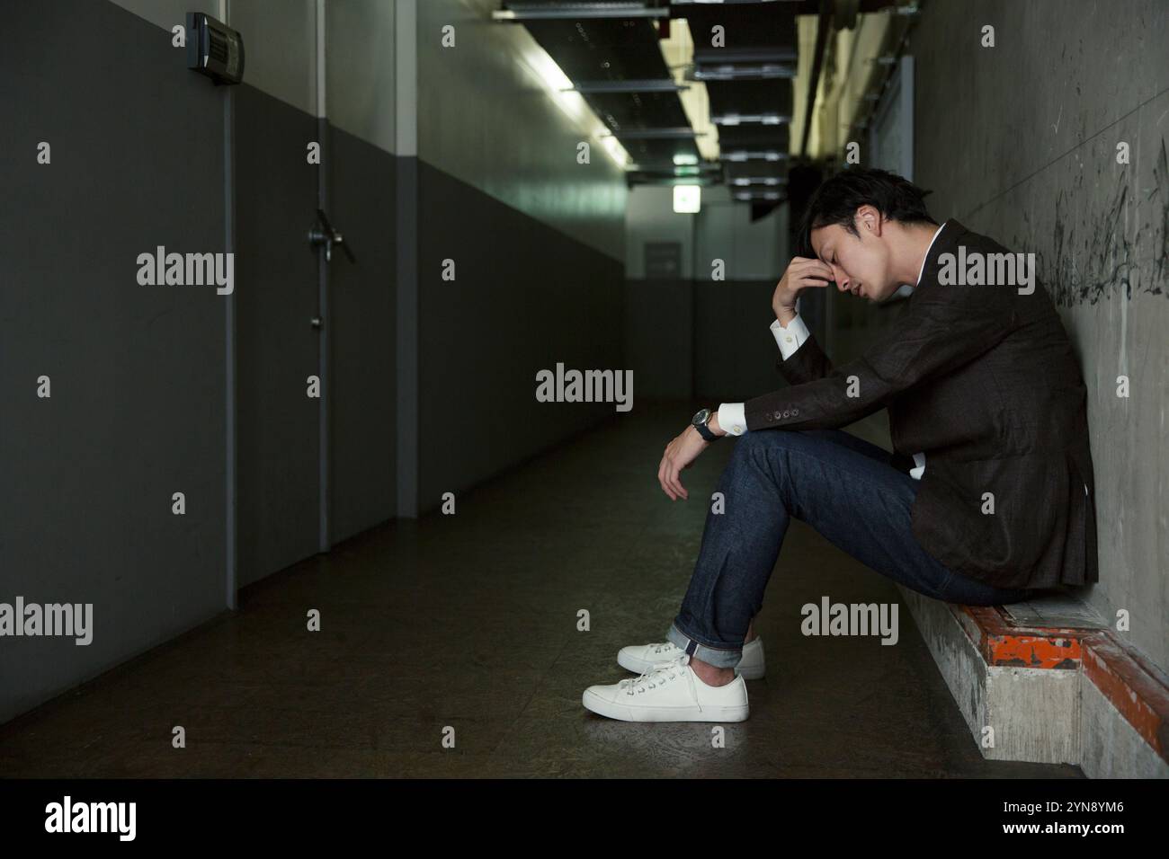 Man crouching and pondering in dark corridor Stock Photo - Alamy