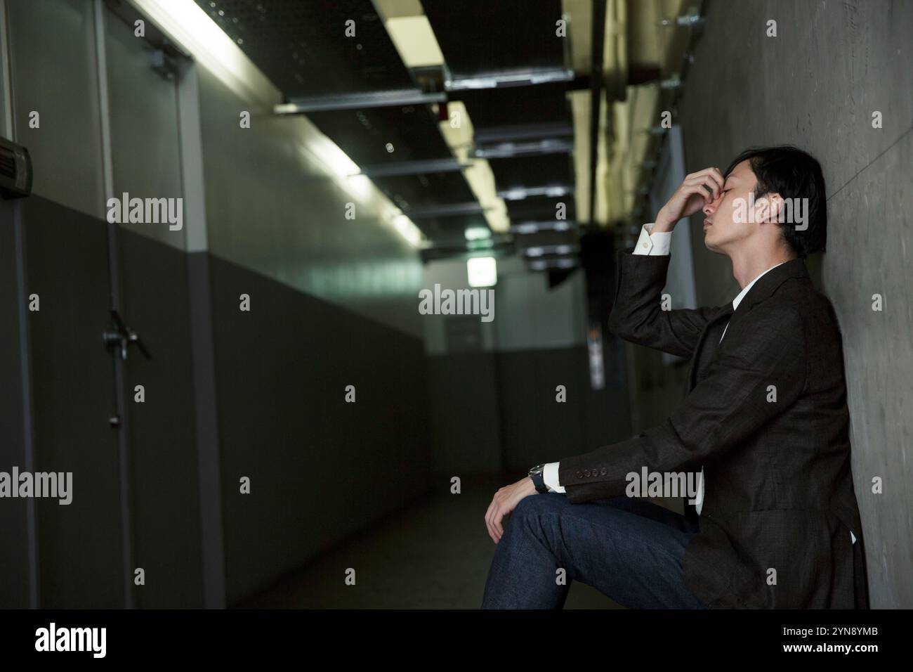 Man crouching and pondering in dark corridor Stock Photo - Alamy