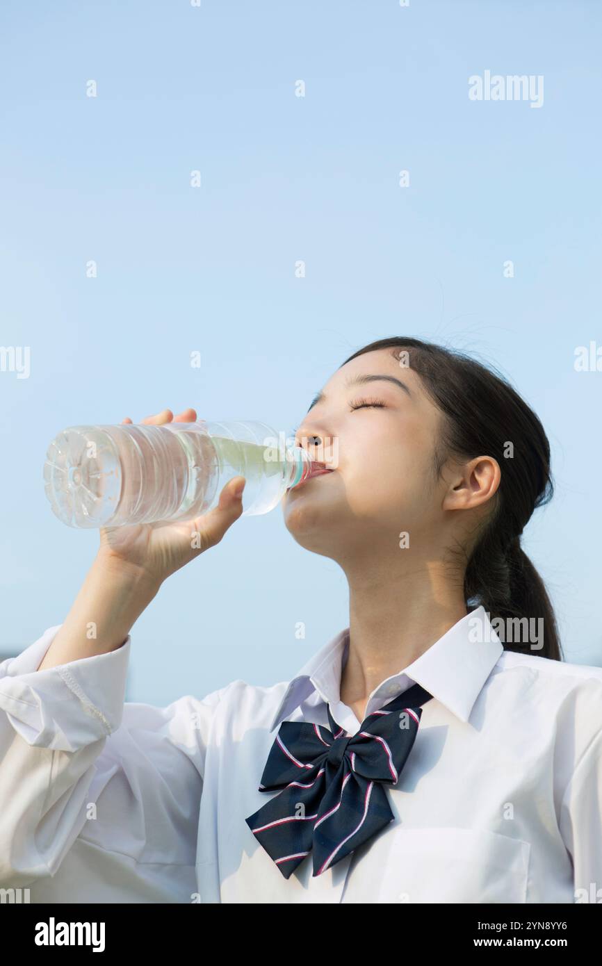 High school girl drinking water from a plastic bottle under a blue sky Stock Photo - Alamy