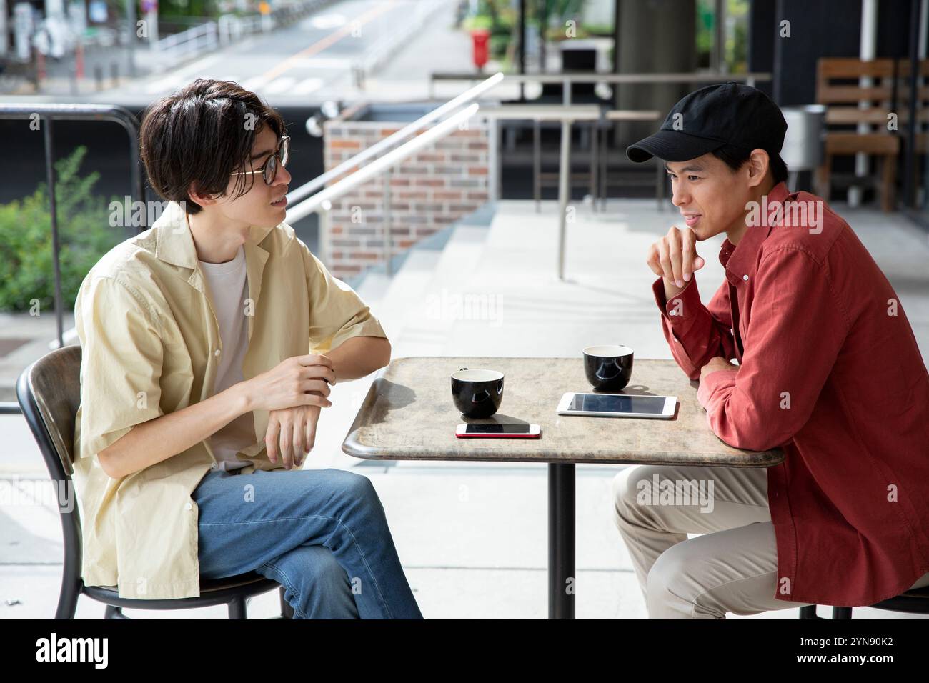 Two men in their 20s talking at a café Stock Photo - Alamy