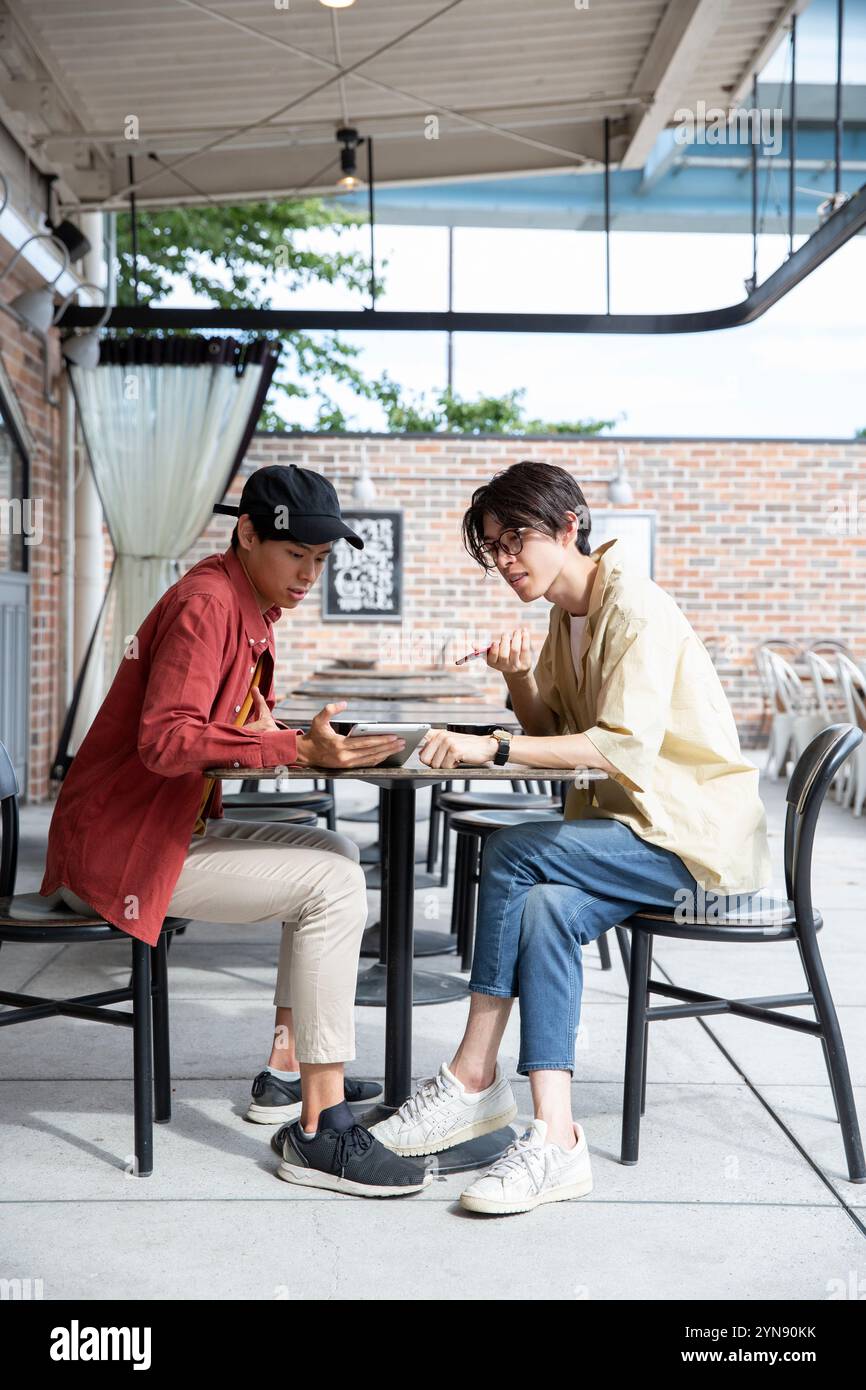Two men in their 20s showing and talking on tablets at a café Stock ...