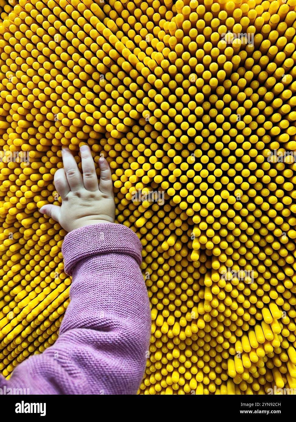 A child's hand touches a bright yellow pin wall, creating a playful ...