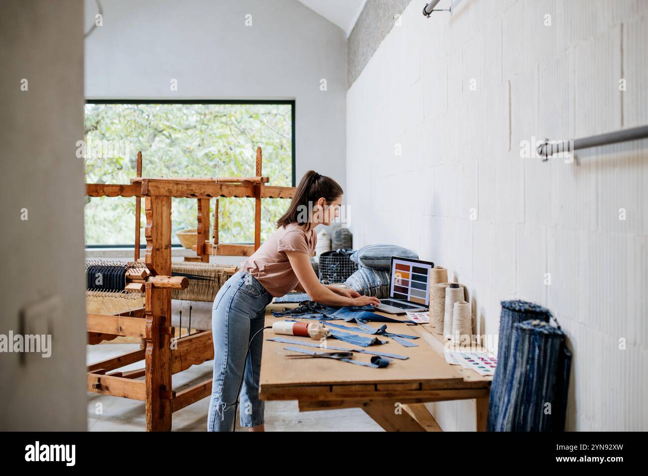 Young businesswoman working on laptop on workbench, standing by wooden ...