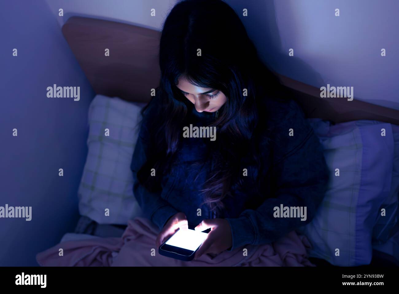 Sad and tired teenager girl using a smartphone lying in bed late at ...