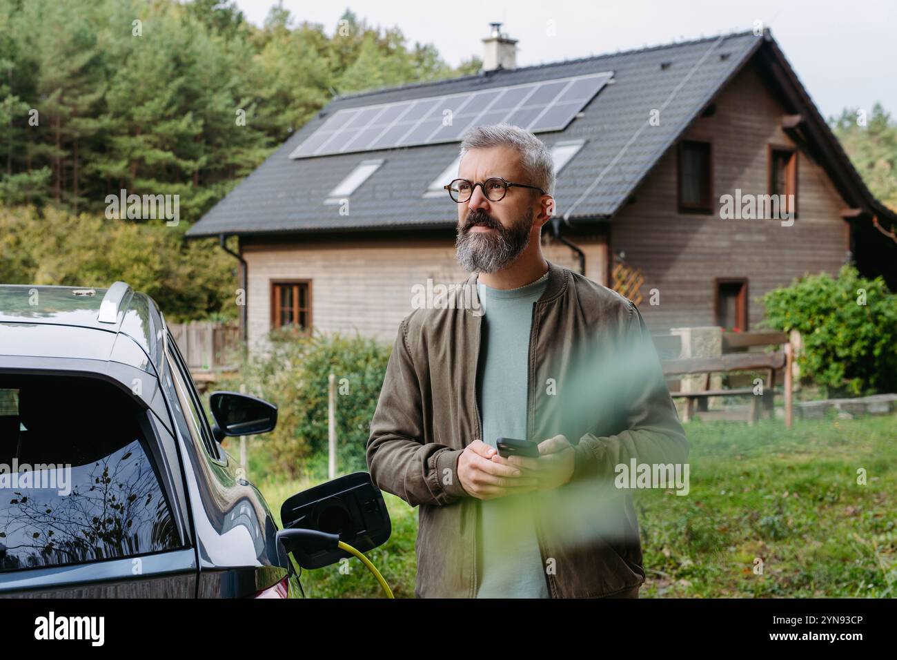 Man charging electric car in front of his house, plugging the charger ...