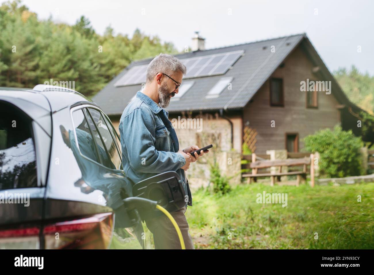 Man charging electric car in front of his house, plugging the charger ...