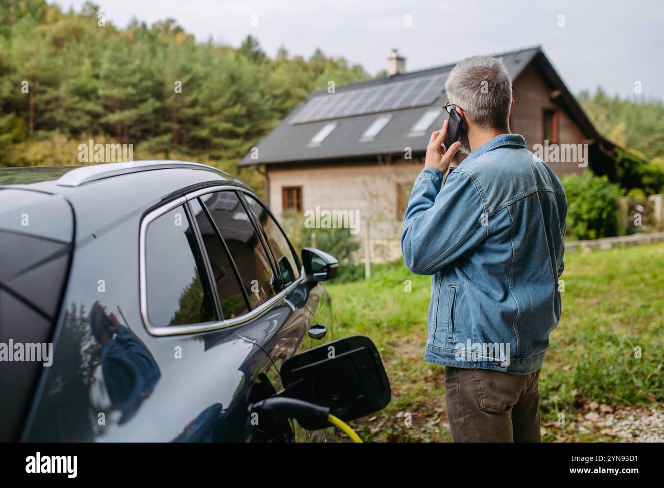 Man charging electric car in front of his house while making phone call ...