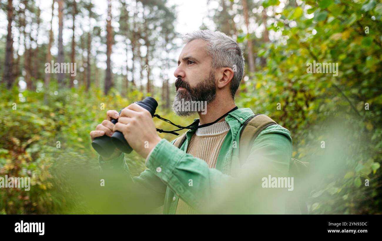 Tourist standing in the middle of nature, using binoculars to observe ...