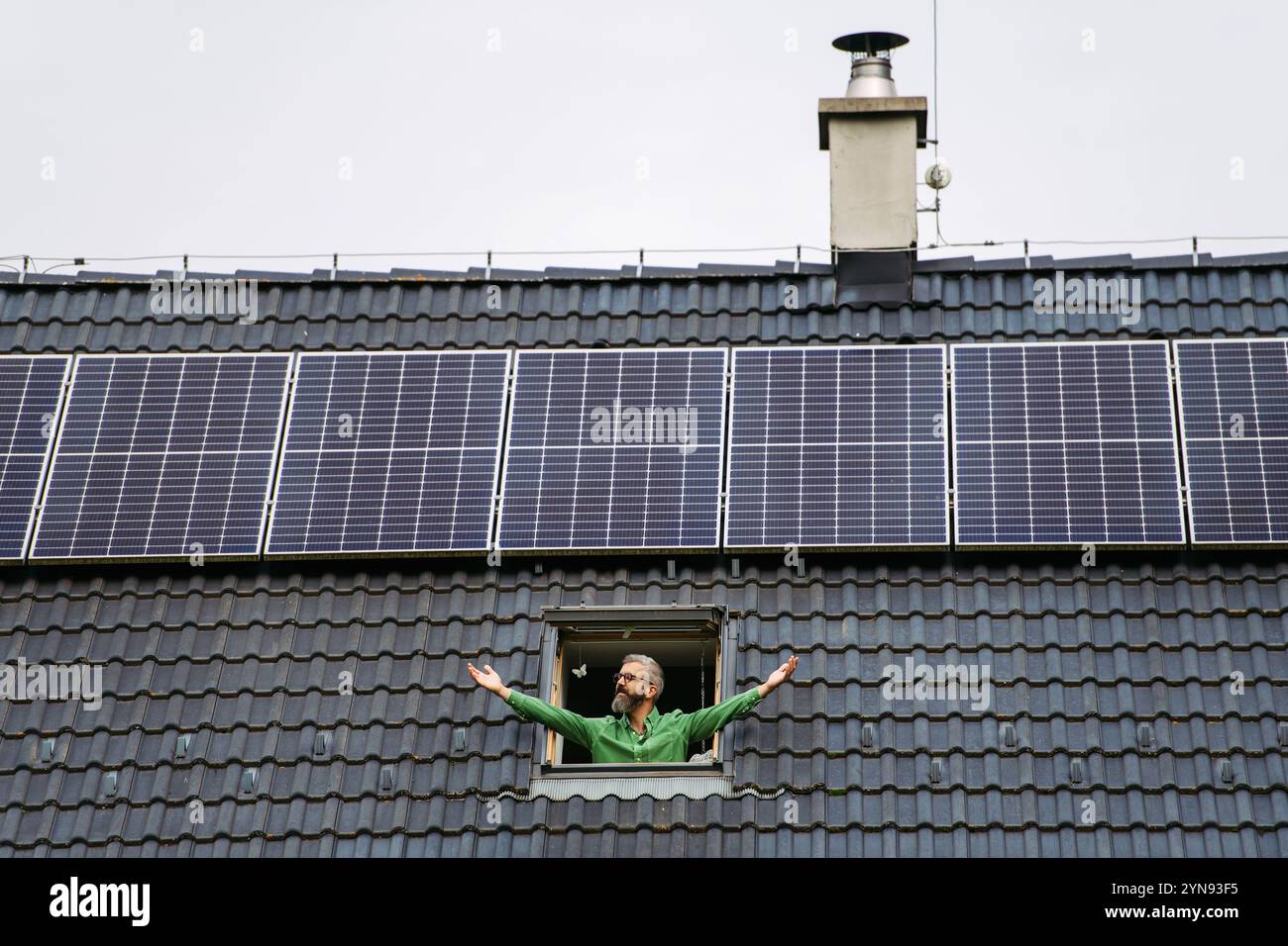 Man looking from skylight, roof window with solar panels above him ...