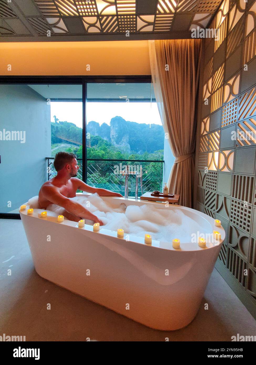 A person enjoys a tranquil bath filled with bubbles, surrounded by soft ...