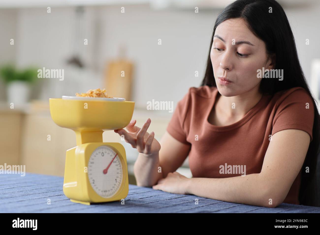 Asian woman weighing food tricking the scale in the kitchen at home ...