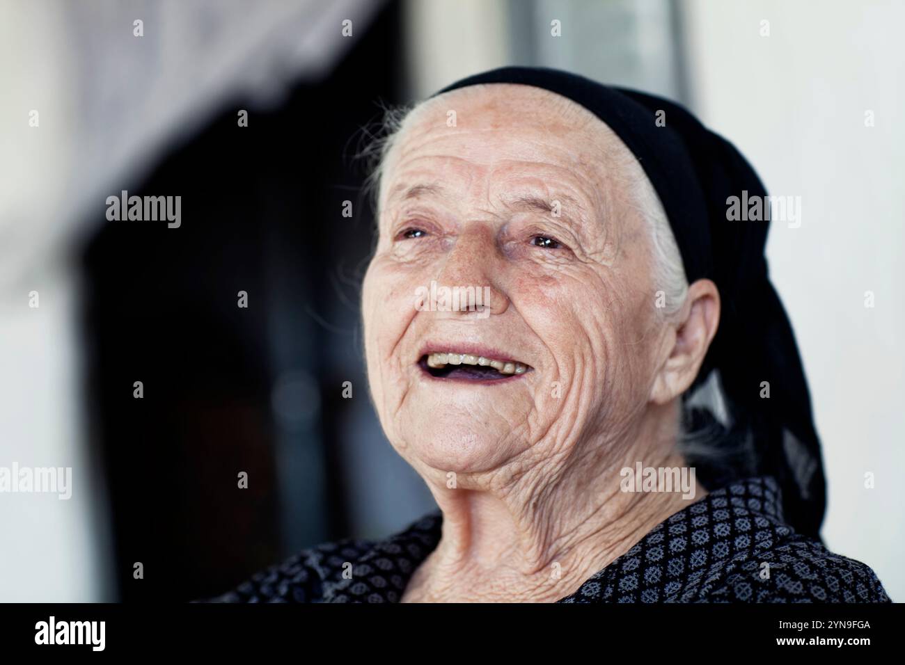 An elderly woman with a warm smile sits comfortably indoors, wearing a ...