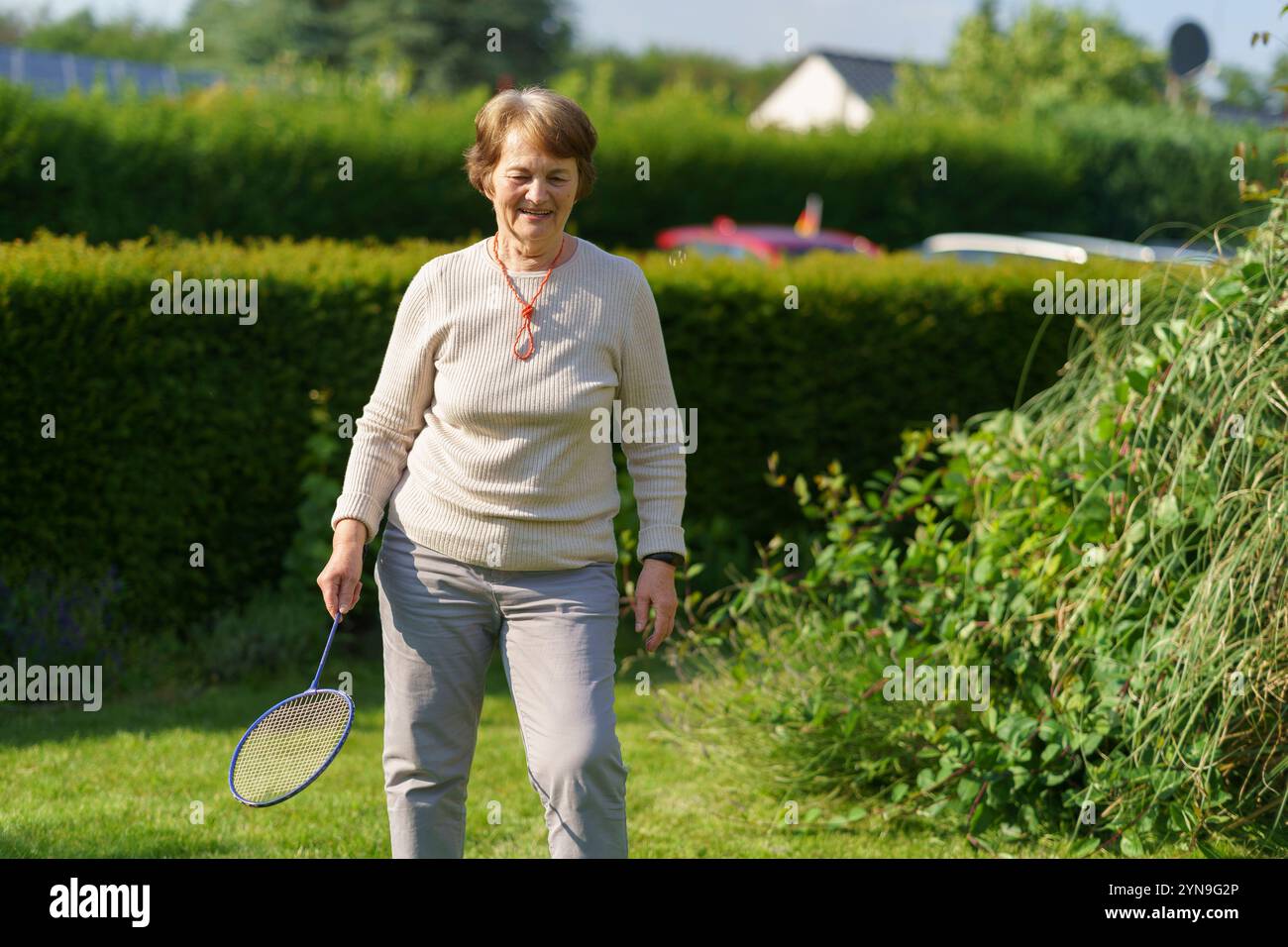 Elderly smiling woman with tennis racket in hand in summer in backyard ...