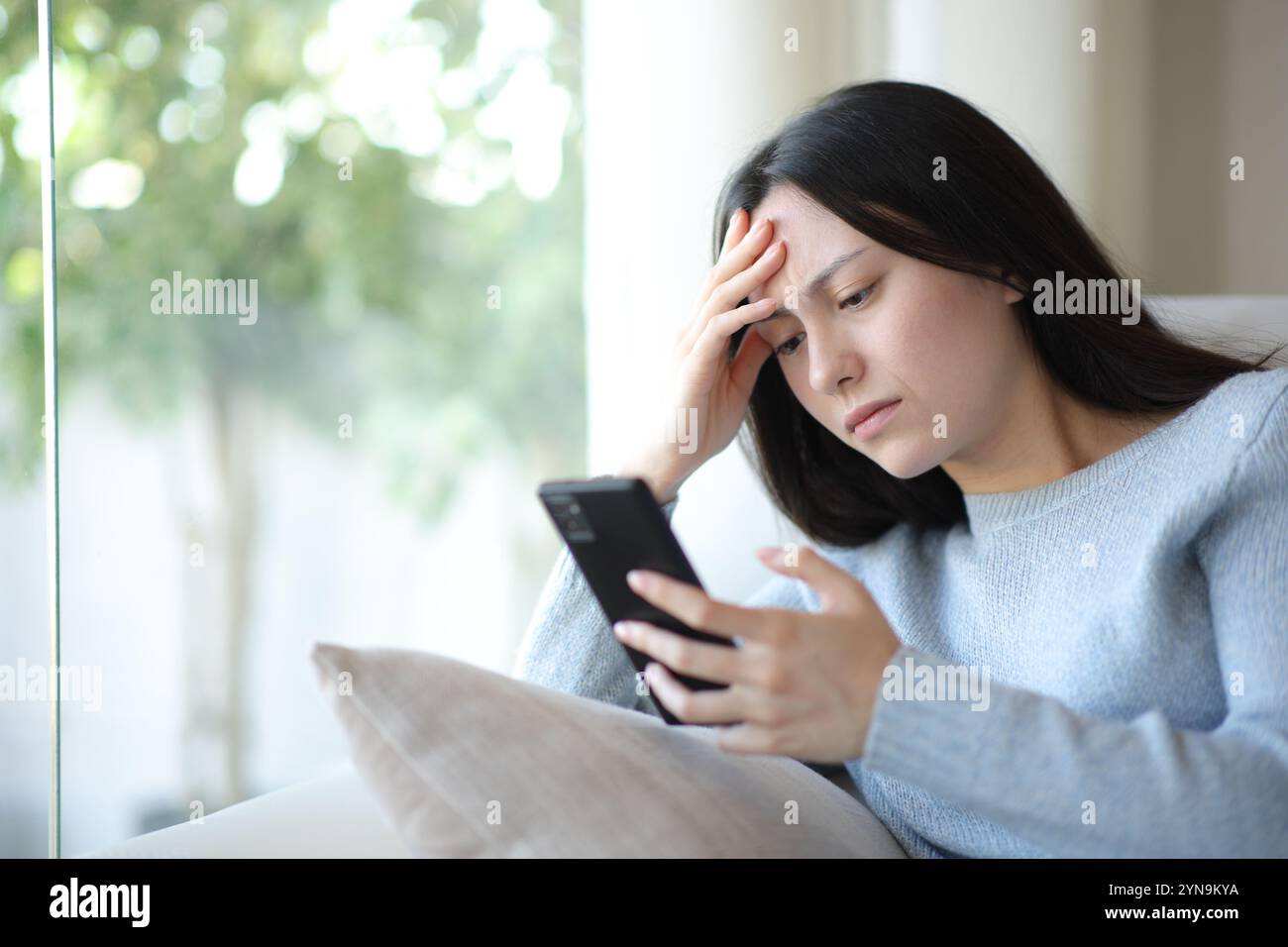 Worried asian woman checking cell phone sitting on a couch at home ...