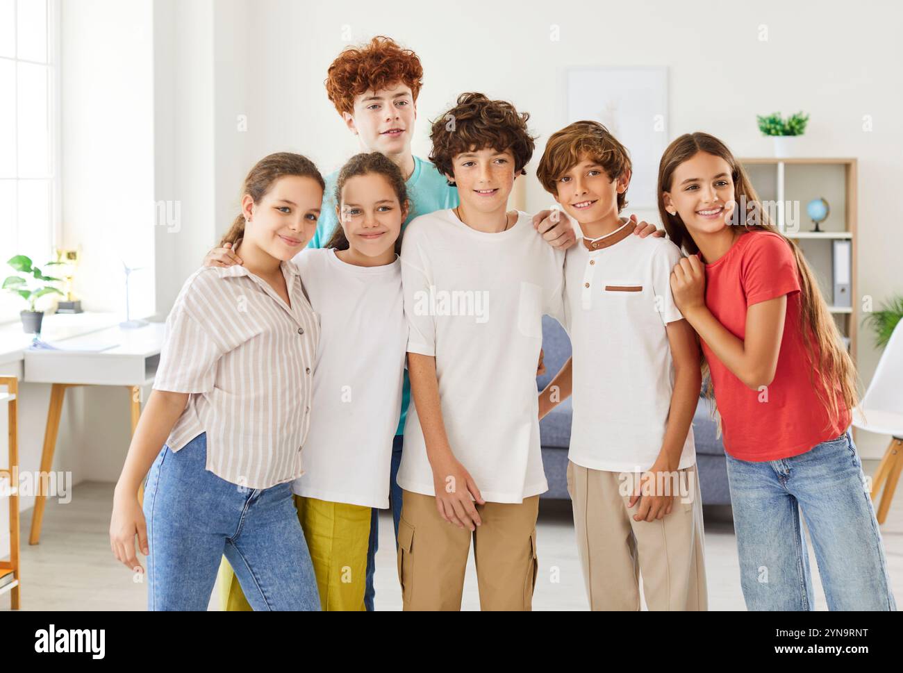 Happy school or college students standing together in classroom looking at camera and hugging ...