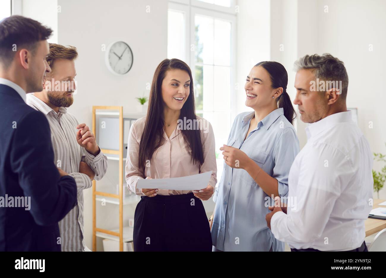 A group of office employees stand at their workplace and communicate ...