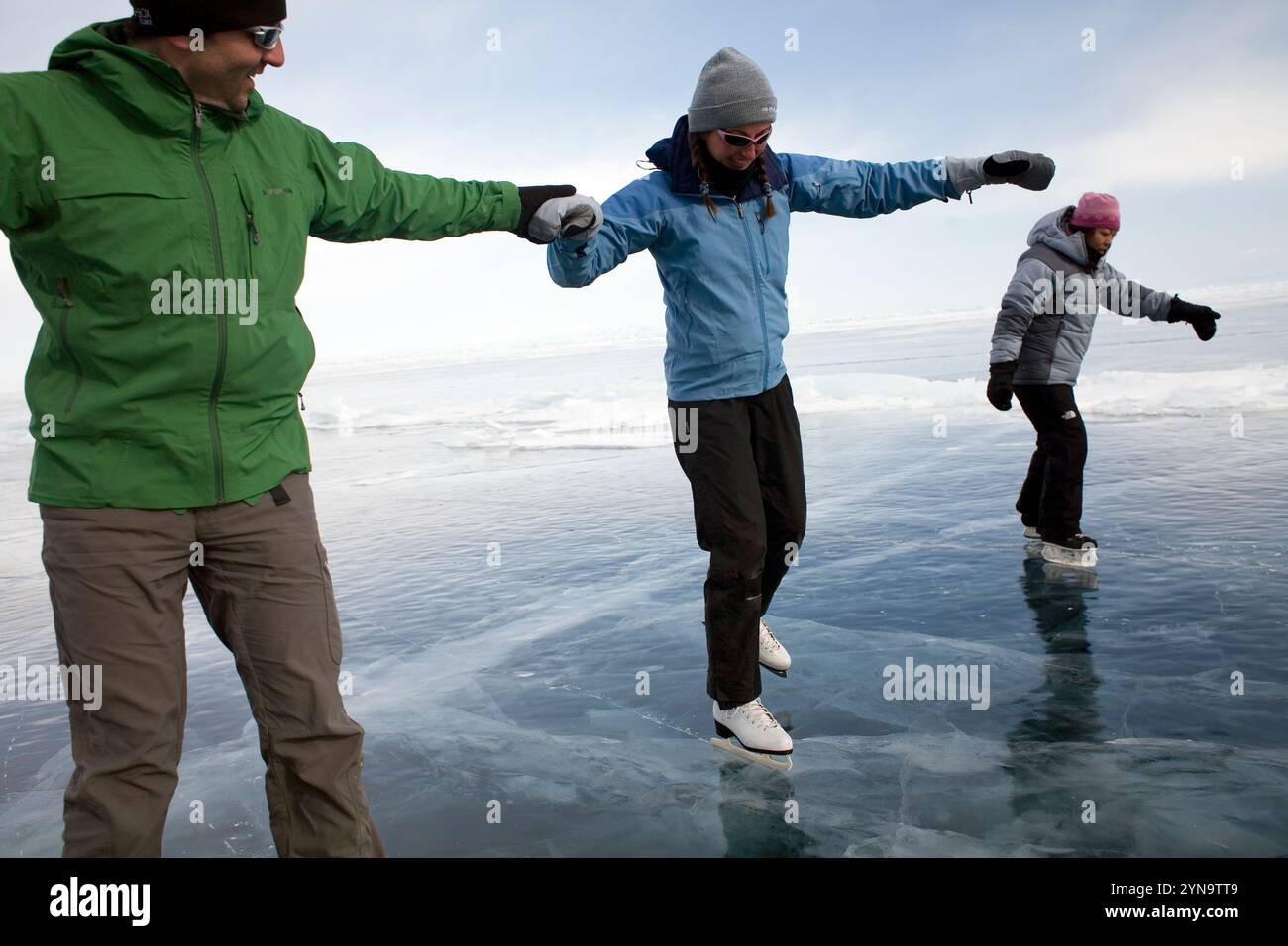 Three people ice skating on the frozen lake Baikal, Siberia, Russia ...