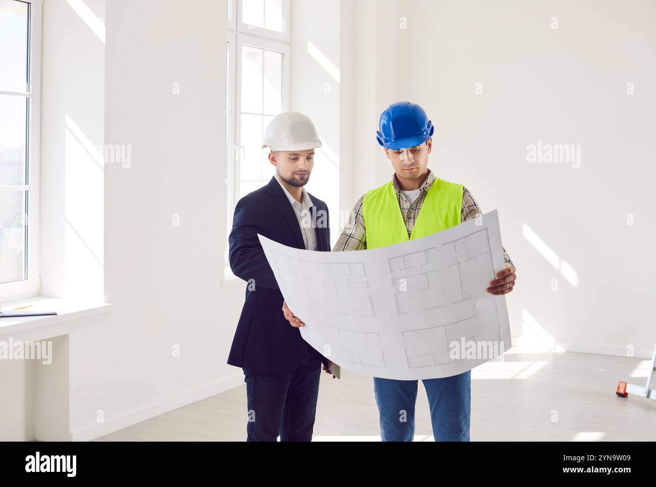 Male builder and engineer standing in apartment, looking at project ...