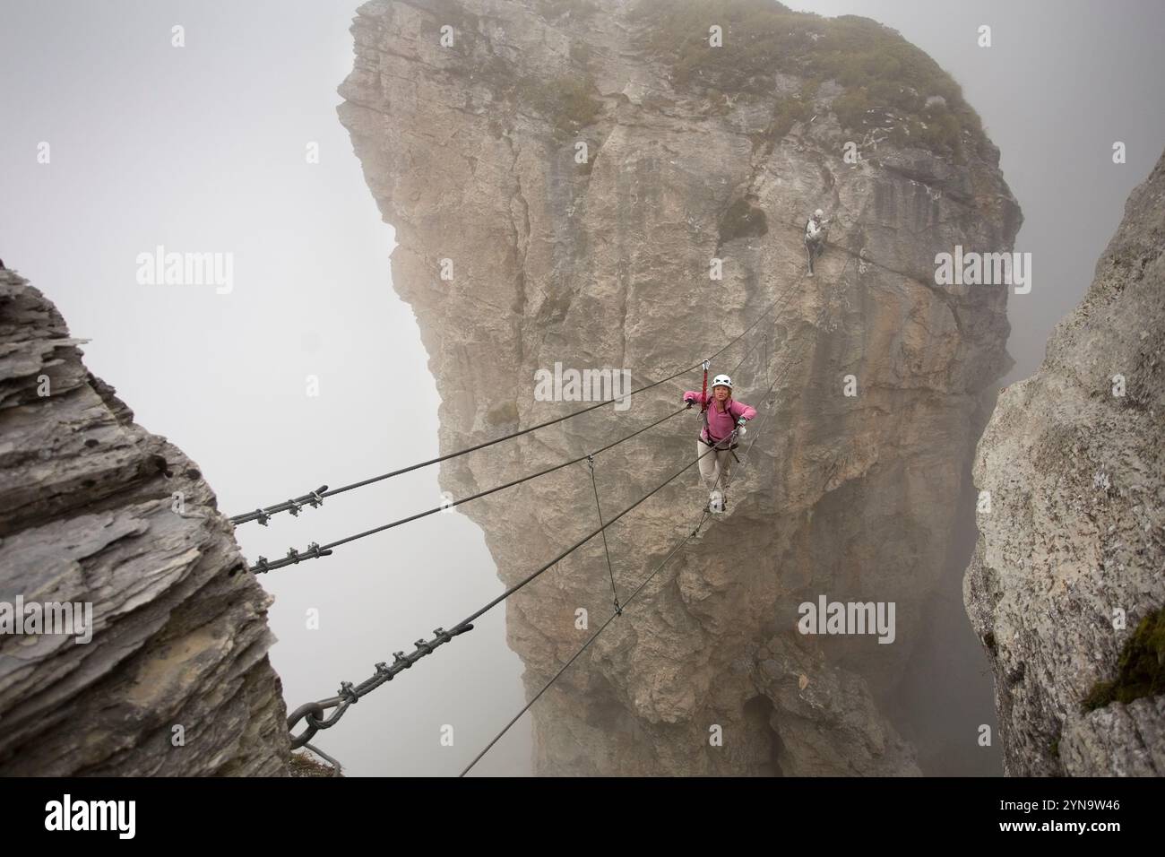 A woman walking across the tight cable bridge section of a Via Ferrata ...