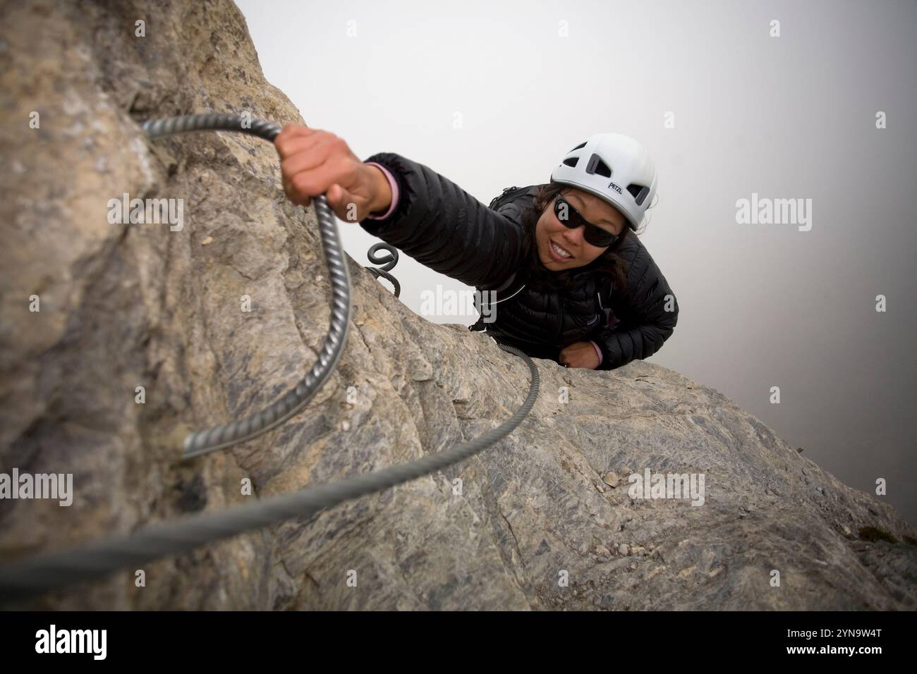 A young woman reaching for a handle embedded in the rock while engaging ...