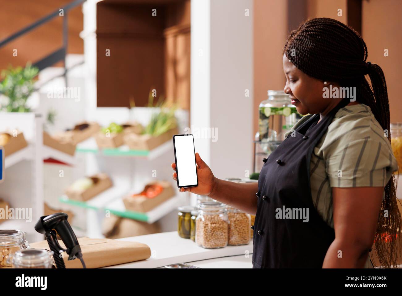 Female storekeeper holds and looks at cellphone with a blank white ...