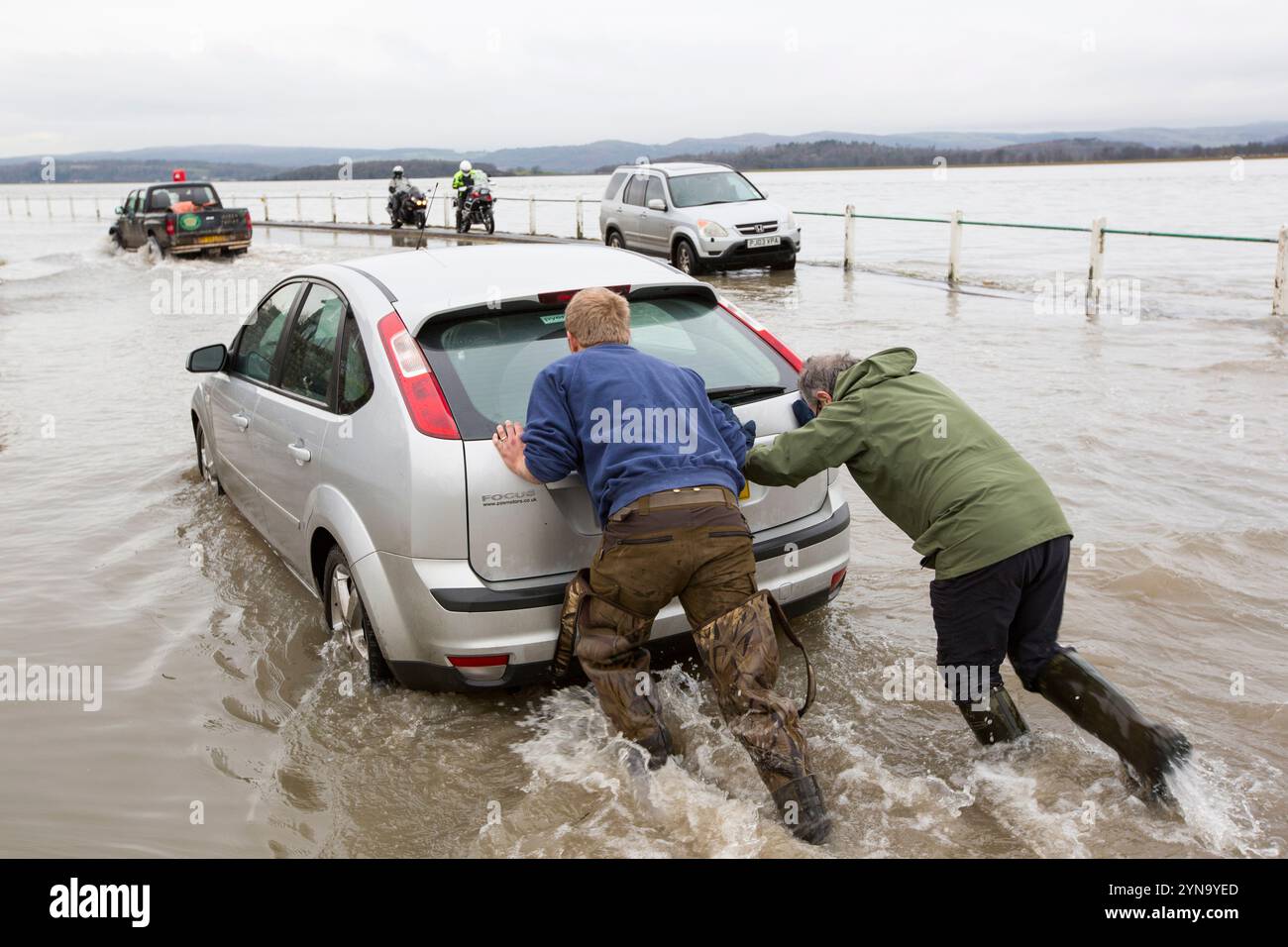Men pushing car stuck in flood in Storth at Kent river estuary Stock ...
