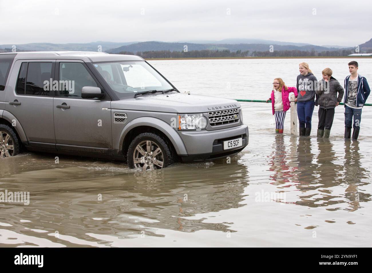 Children watching car driving through flooded street in Storth at Kent ...