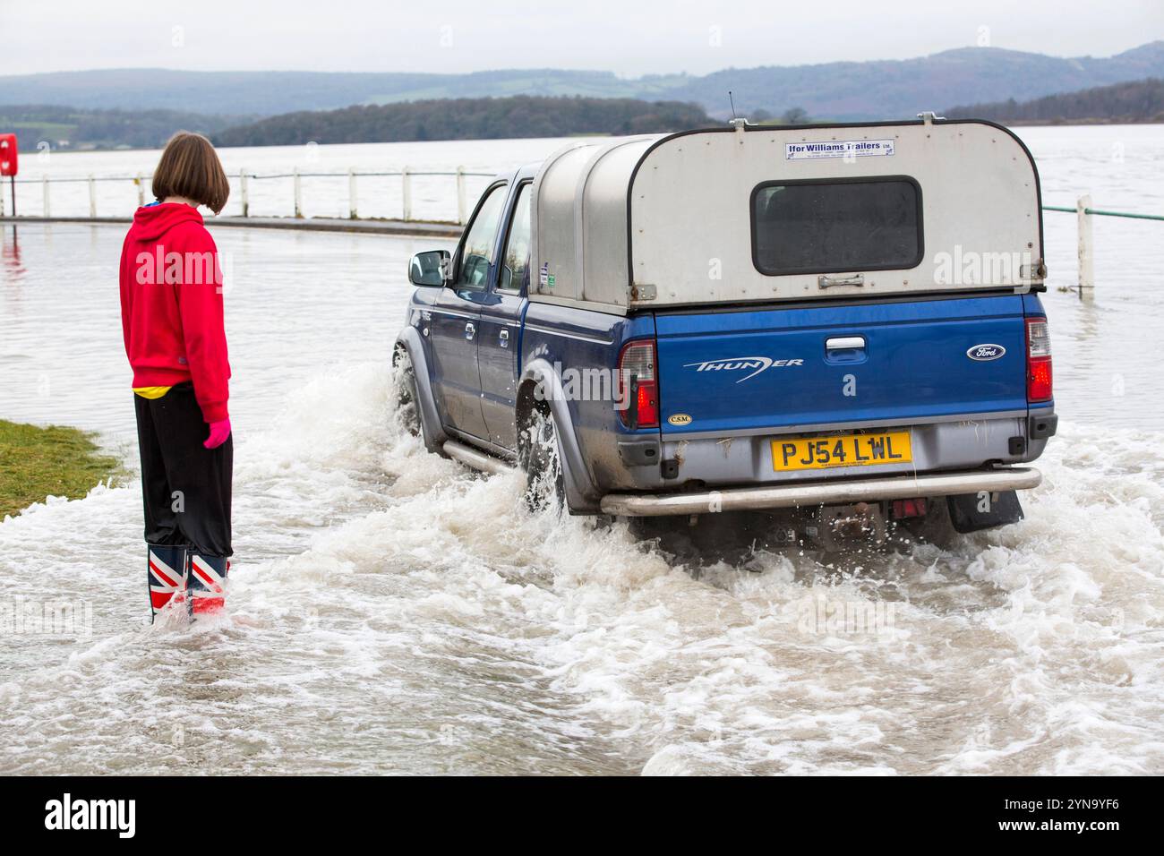 Woman watching car driving in flooded street in Storth at Kent river ...