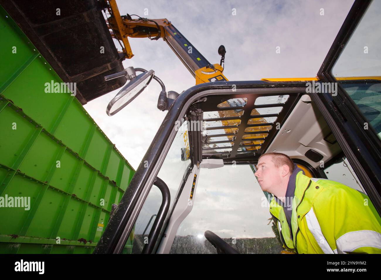 Young man driving bulldozer loading organic waste into tank at ...