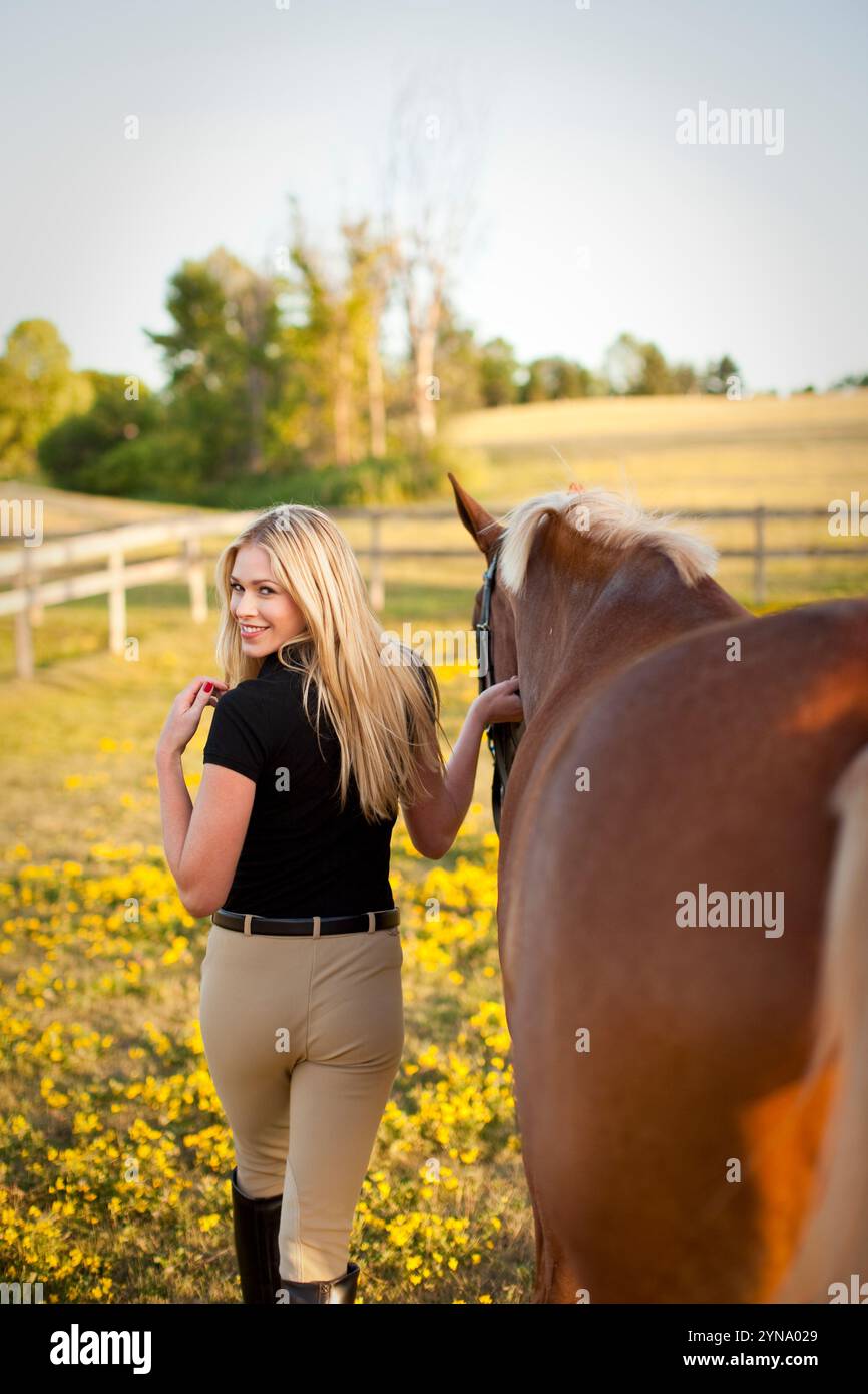 A woman walks away with a horse in a flowered stable during a lifestyle ...