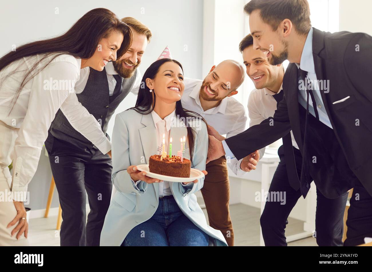 Team of people celebrating a colleague's birthday, giving her a cake ...