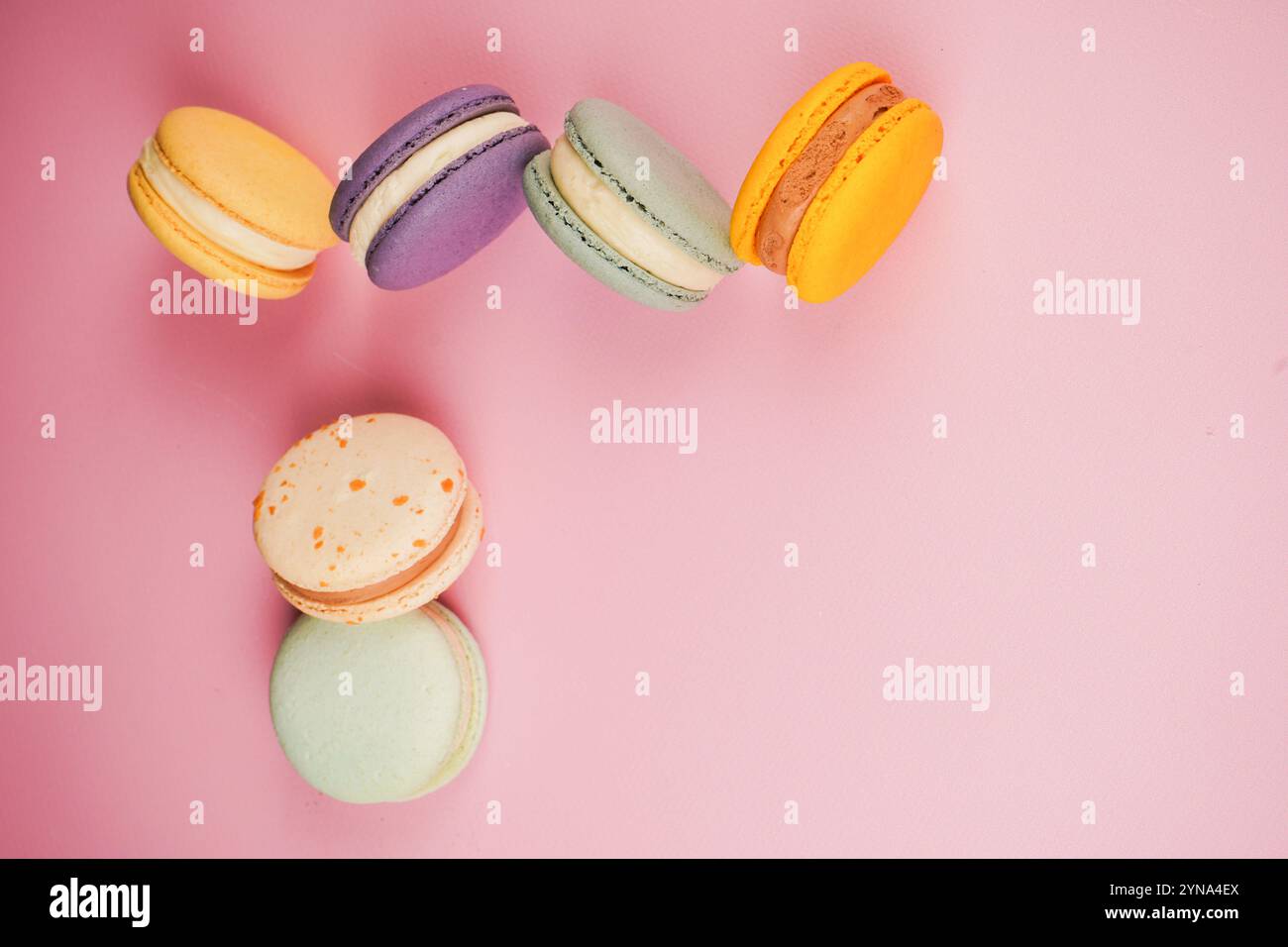 Bright and colorful macarons lined up on a surface with a pink ...