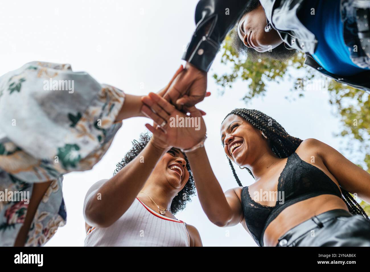 Group of women joining hands together outdoors, smiling and celebrating their friendship and ...