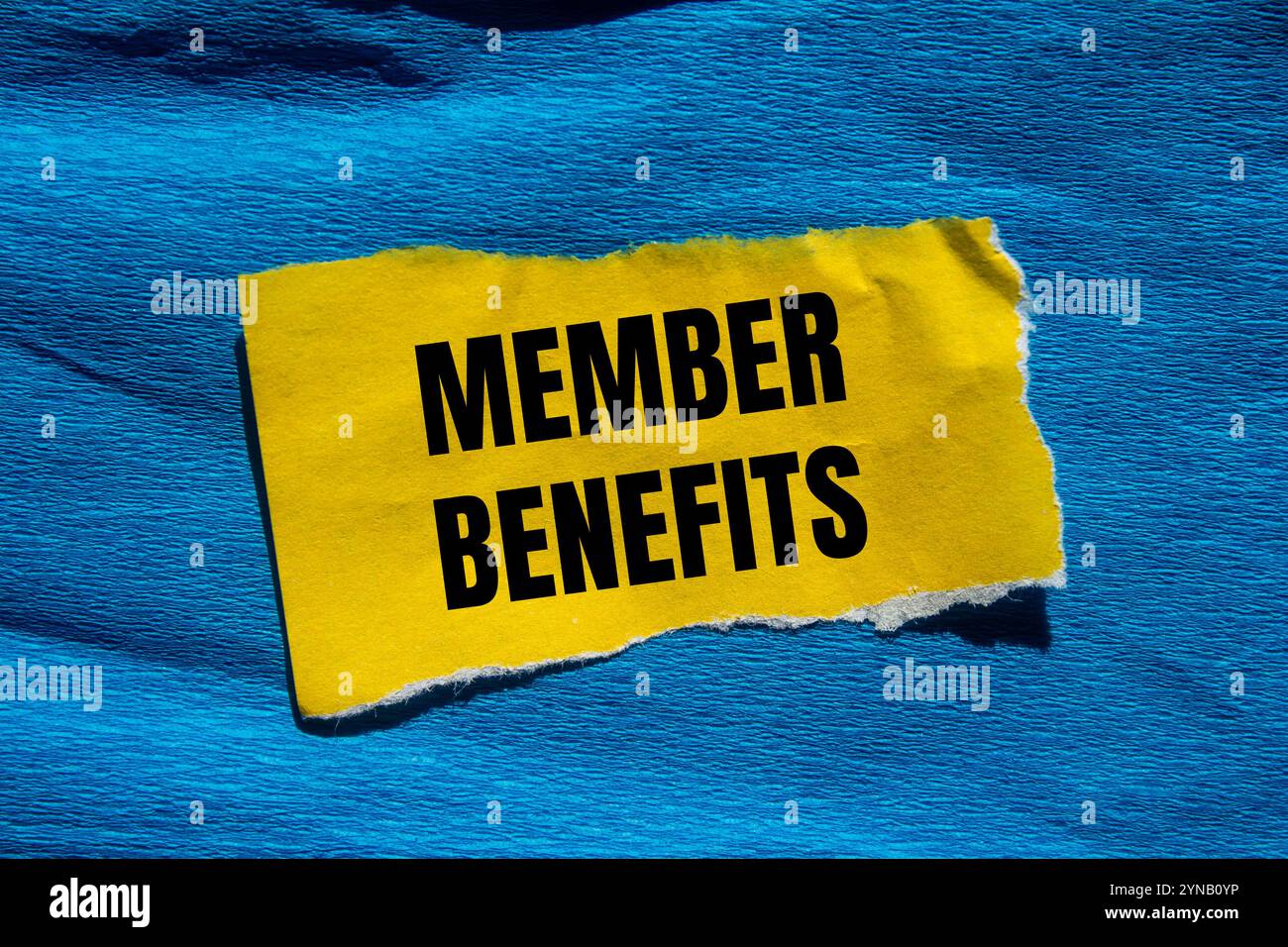 Member benefits message written on ripped torn yellow paper piece with blue background ...