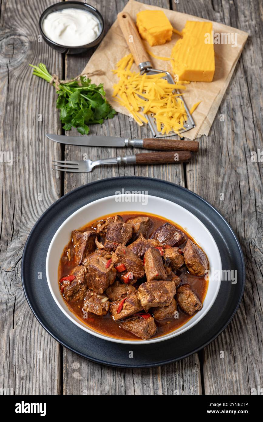 beef stew in a white bowl on rustic wooden table with shredded cheddar ...