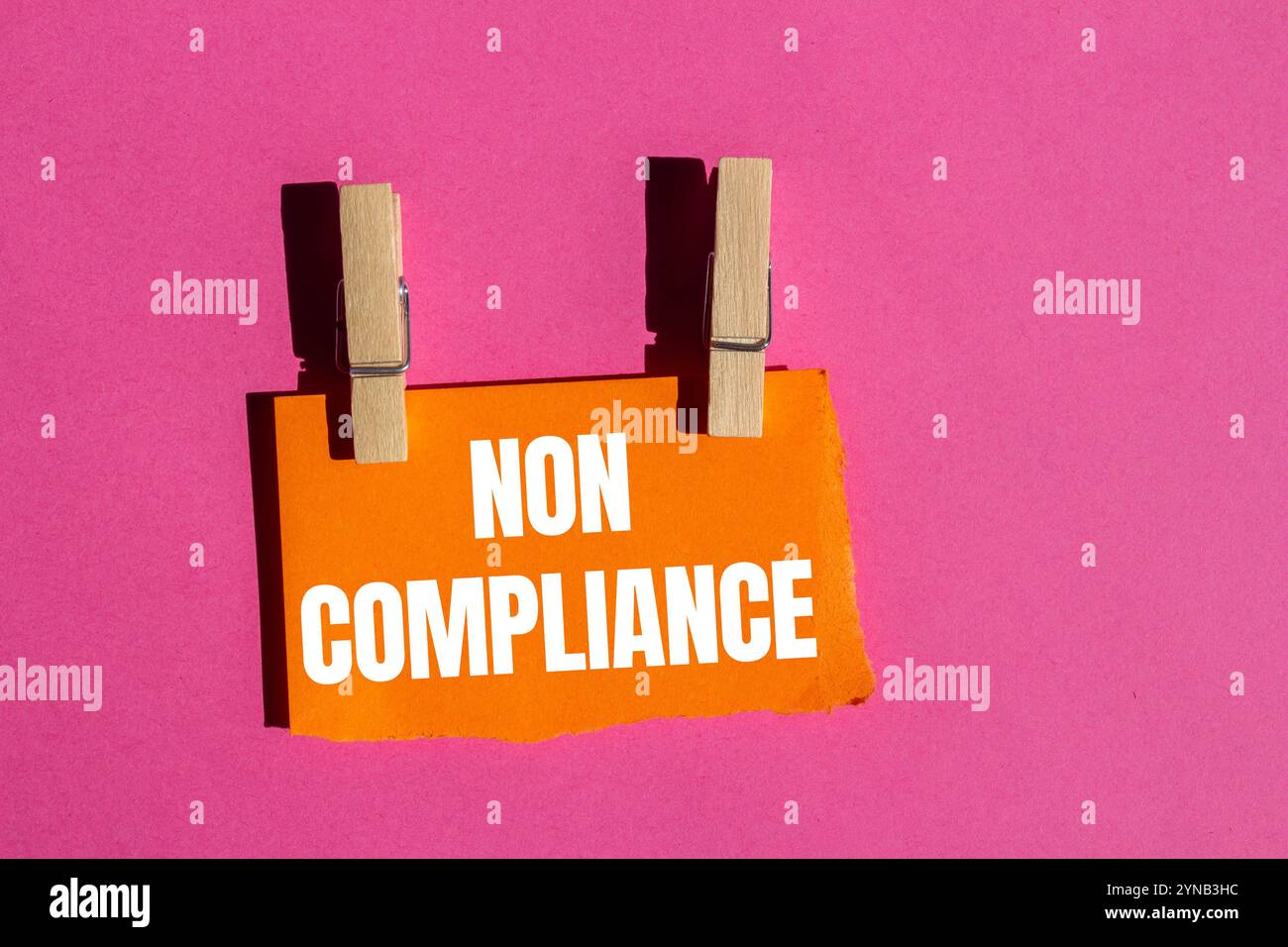 Non compliance message written on ripped torn orange paper piece with pink background ...
